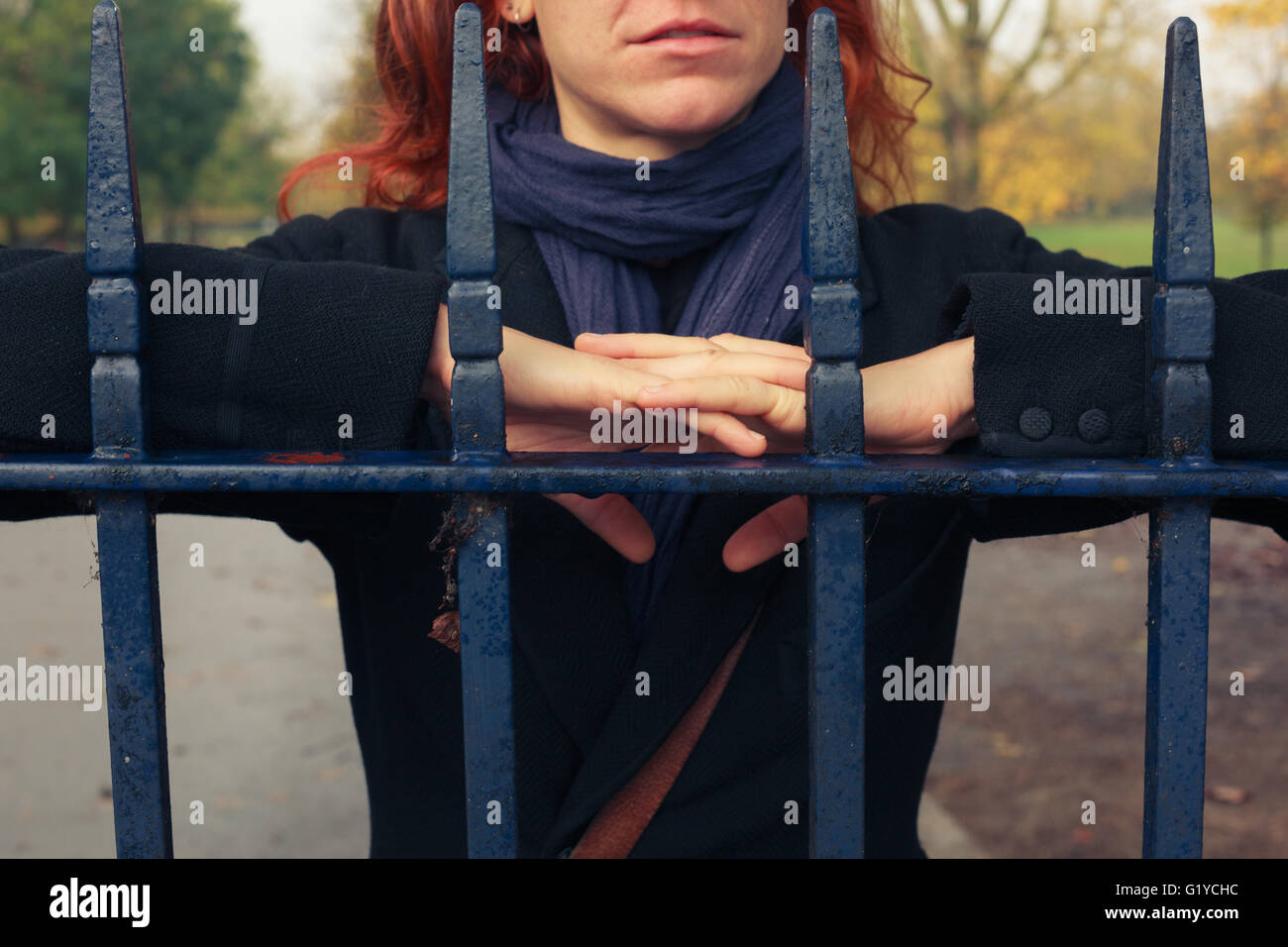 A young woman is leaning on a gate in a park in the autumn Stock Photo ...