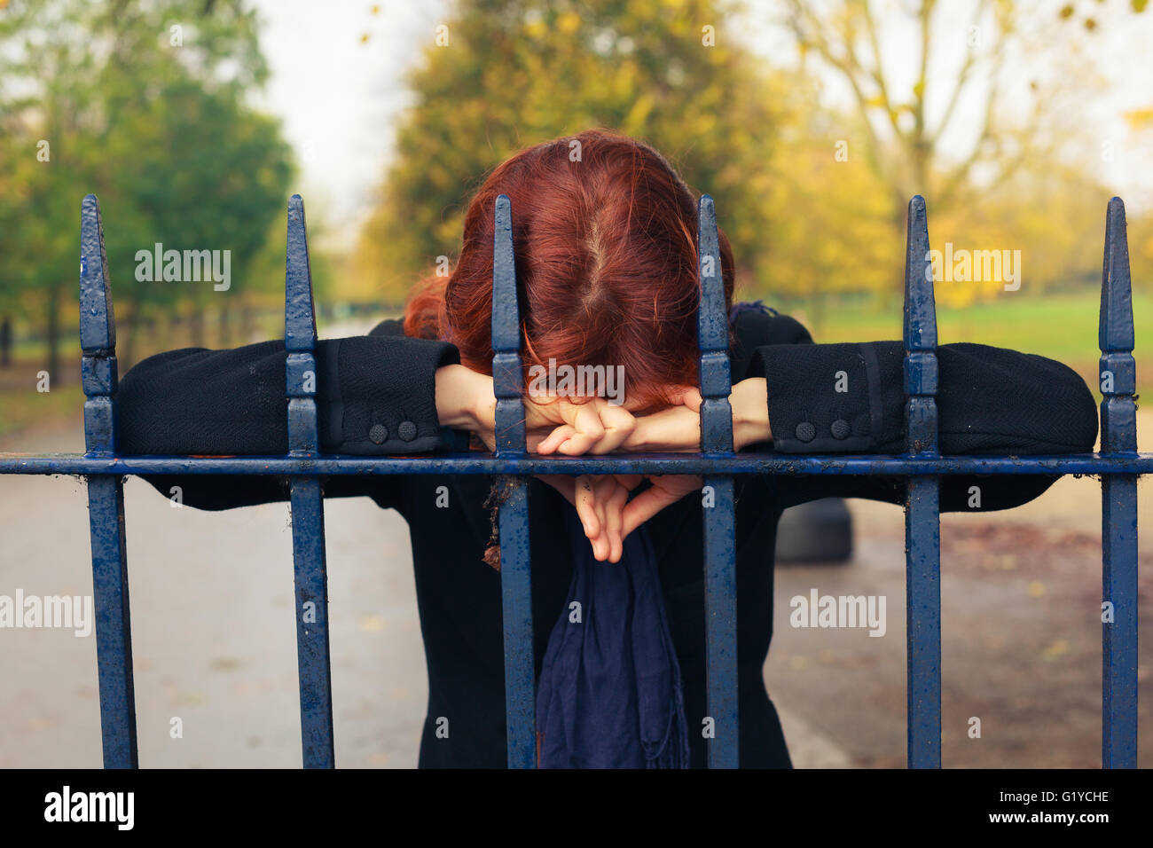 A sad woman is resting her head on a gate in the park in autumn Stock ...