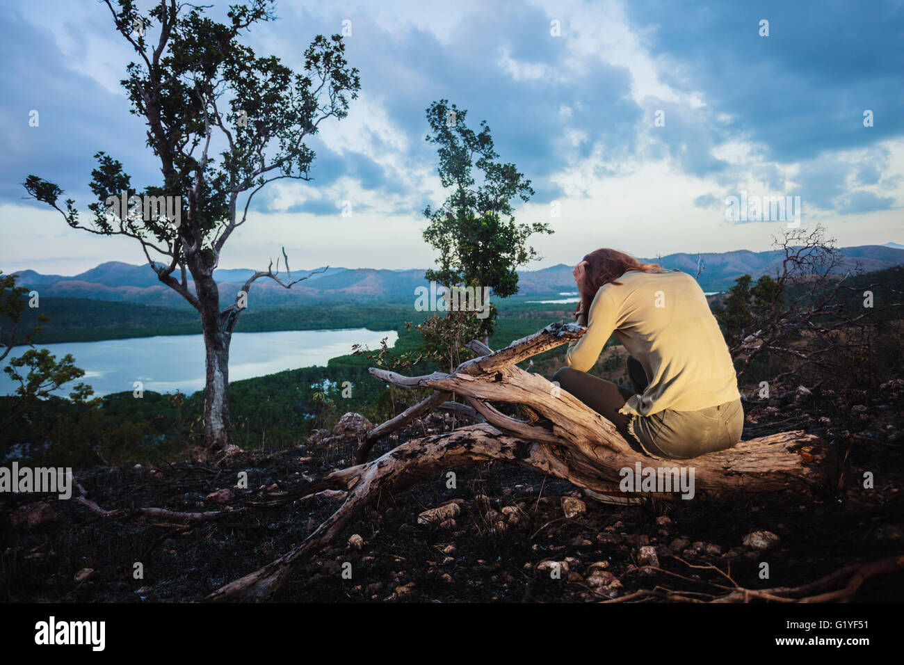 A sad young woman is sitting on a hill burned by a wild fire Stock ...
