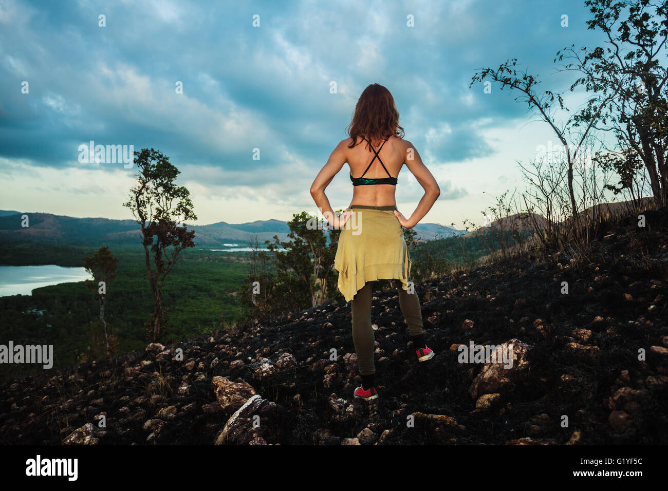 A young woman is standing on a hill scorched by a wild fire in a ...