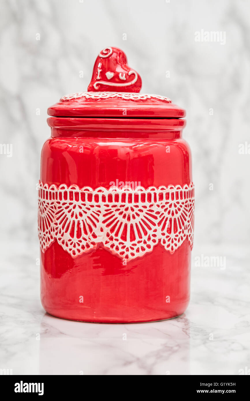 Red round porcelain jar with lace pattern on white marble background ...