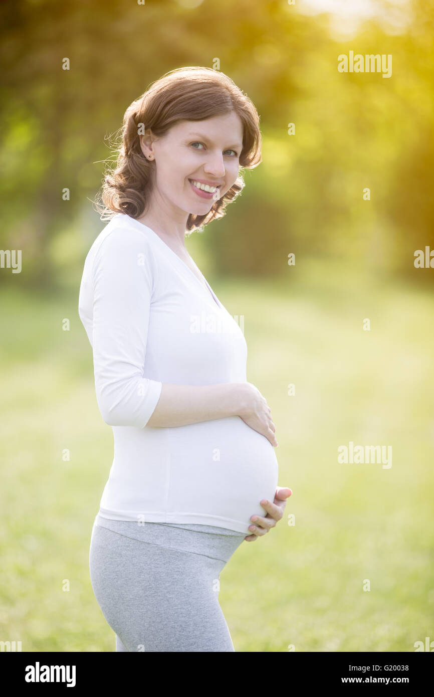 Portrait of happy young pregnant model looking at camera while standing ...
