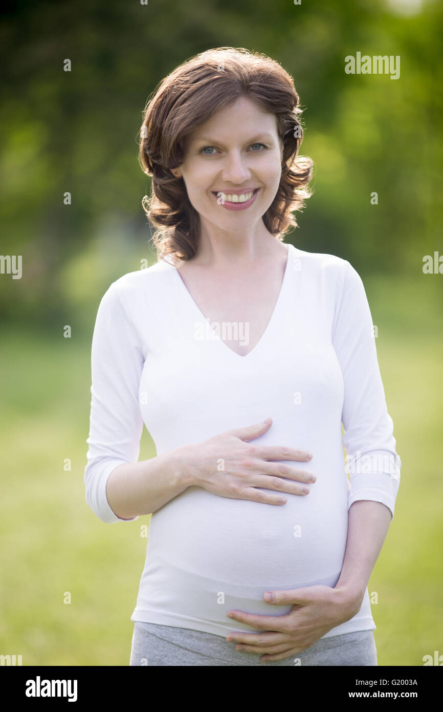 Portrait of happy young pregnant model looking at camera with blissful ...
