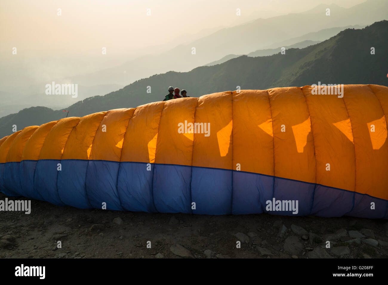 A paraglider rises with the wind in its wings against the setting sun ...
