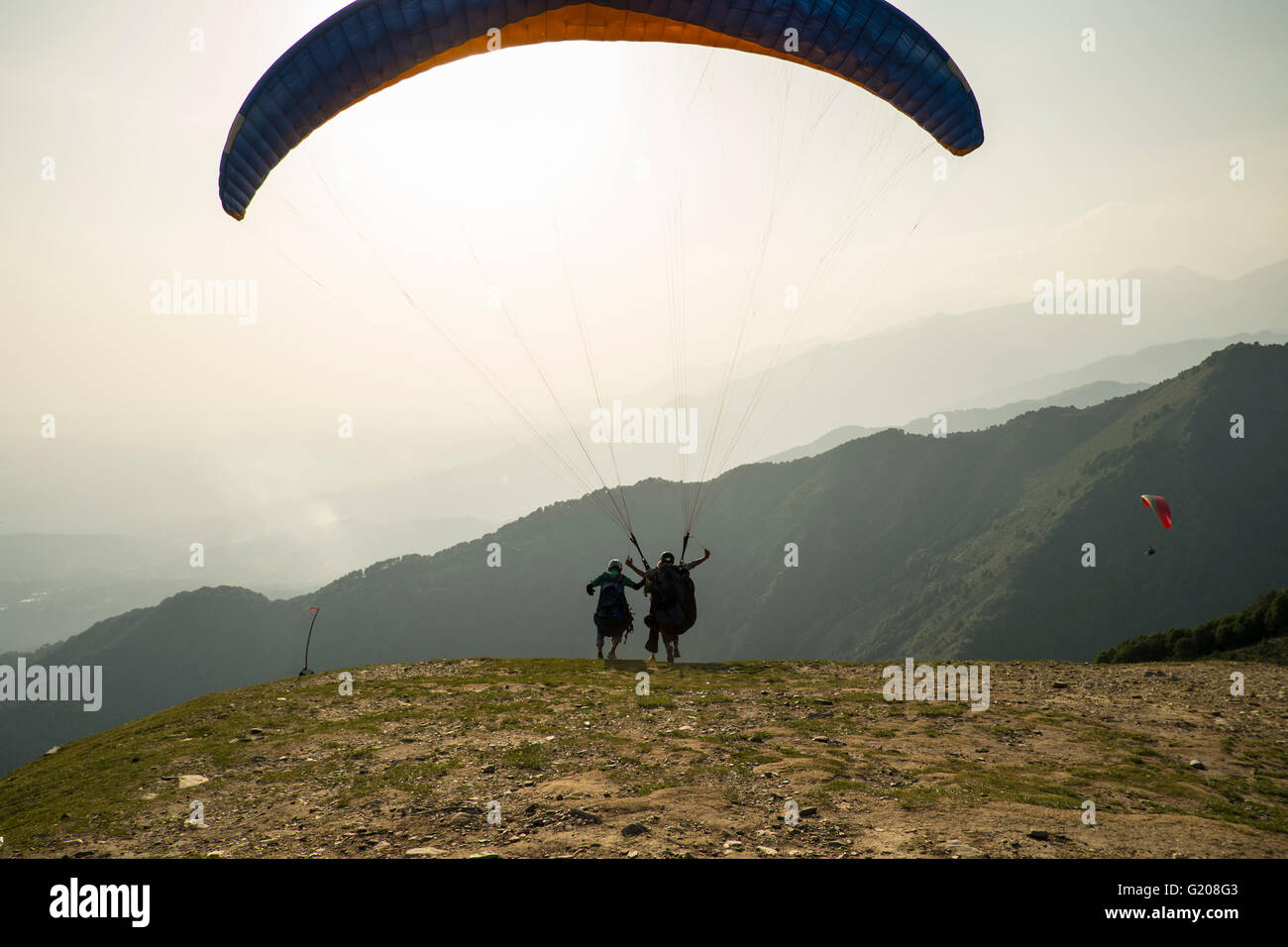 A paragliding instructor helps a glider take off against the sun in ...