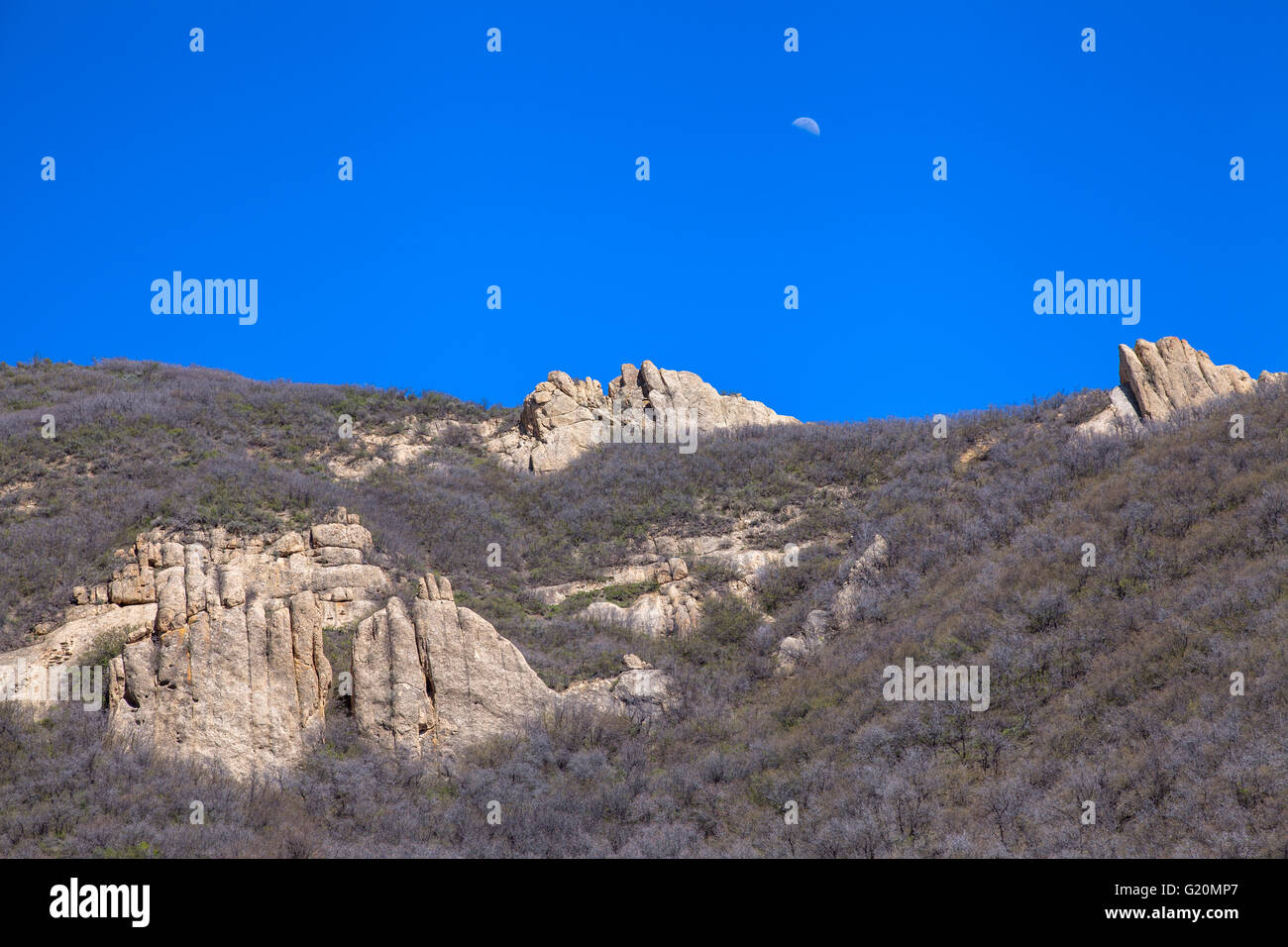 Moon rising above hillside with interesting rock formations Stock Photo ...