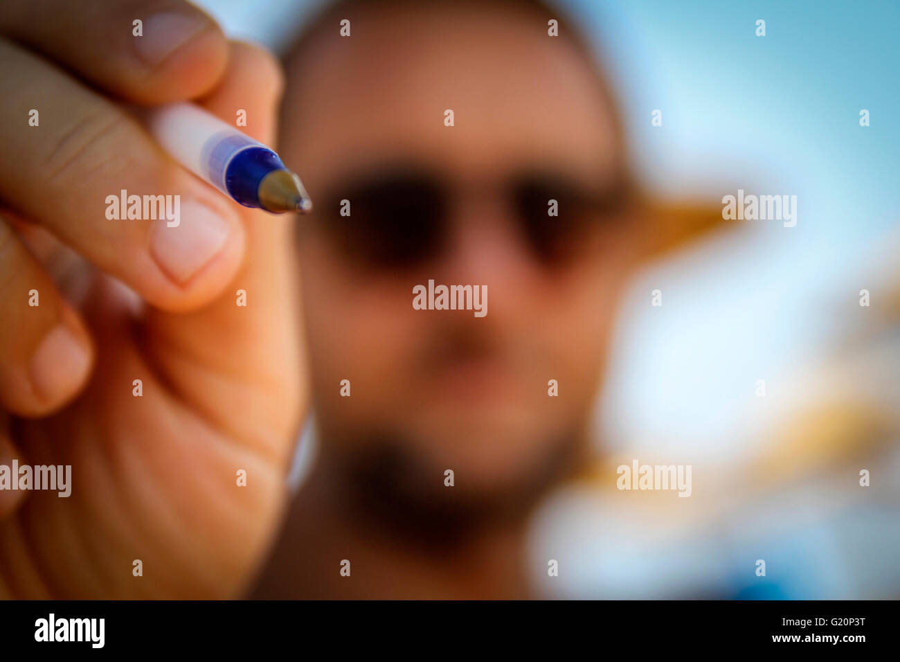 hand holding a pen while the pens ball point is focused and the face of ...