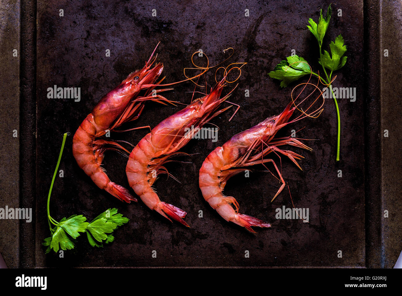 Three prawns on a black stone ready to be cooked with parsley Stock ...