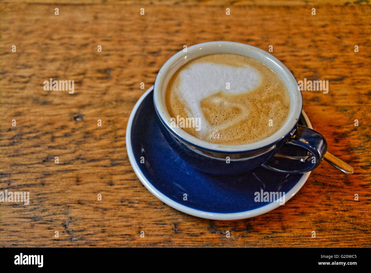 Cup of creamy, milky coffee late, on a brown, wooden table, in a blue ...