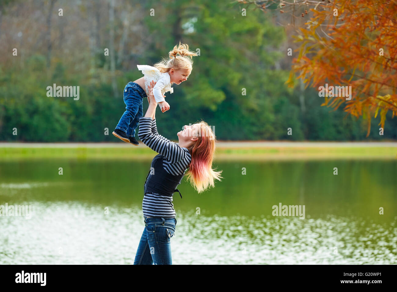 Mother playing throwing up baby girl daughter in the park lake Stock ...