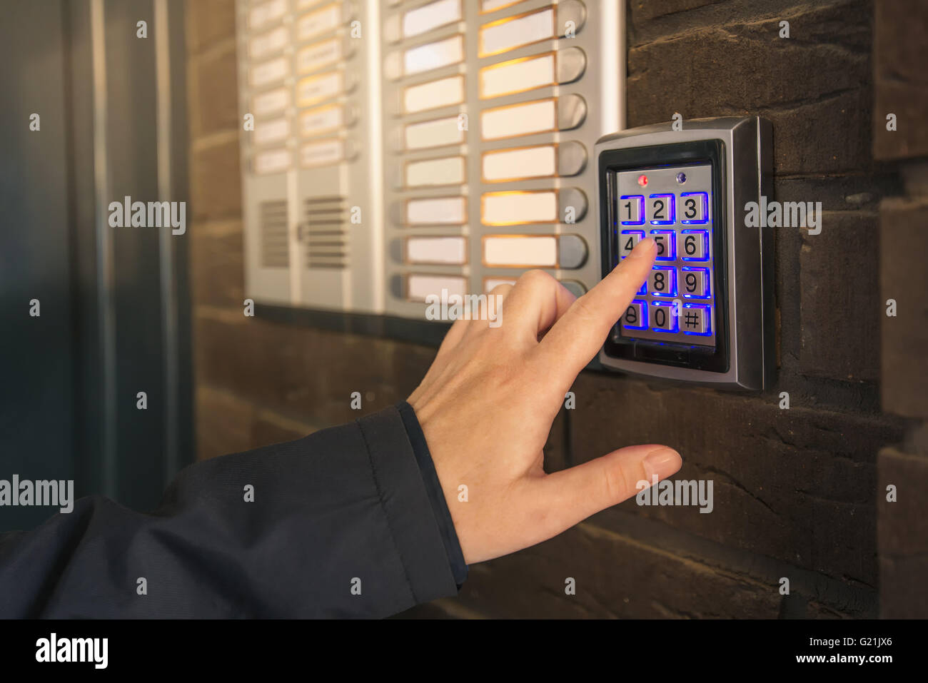 Woman dialing pass code on intercom security keypad to open entrance door of the apartment ...