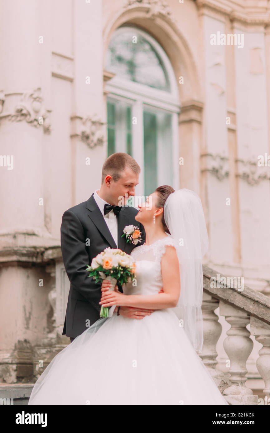 Beautiful married couple smiling and hugging near old building wall ...