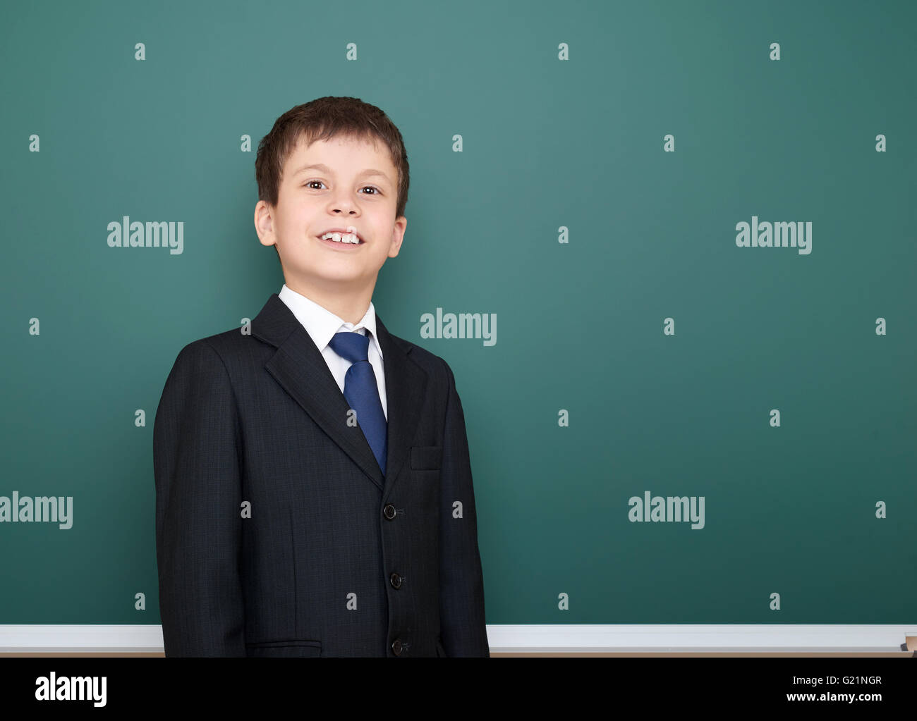 happy successfull school boy in black suit portrait on green chalkboard ...