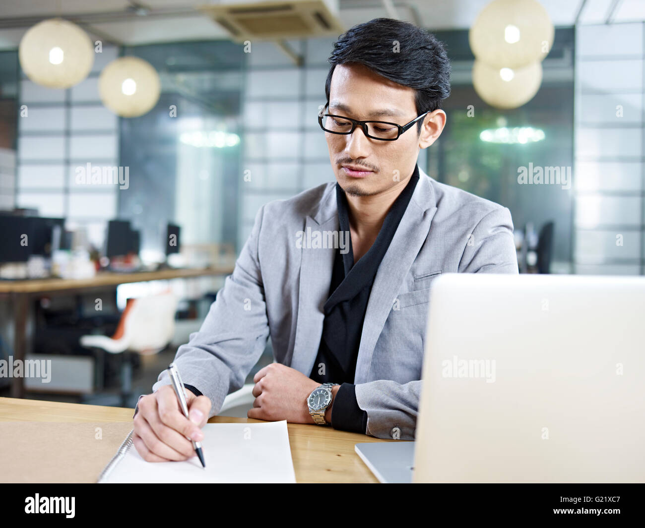 asian business man sitting at desk in office writing on a piece of ...