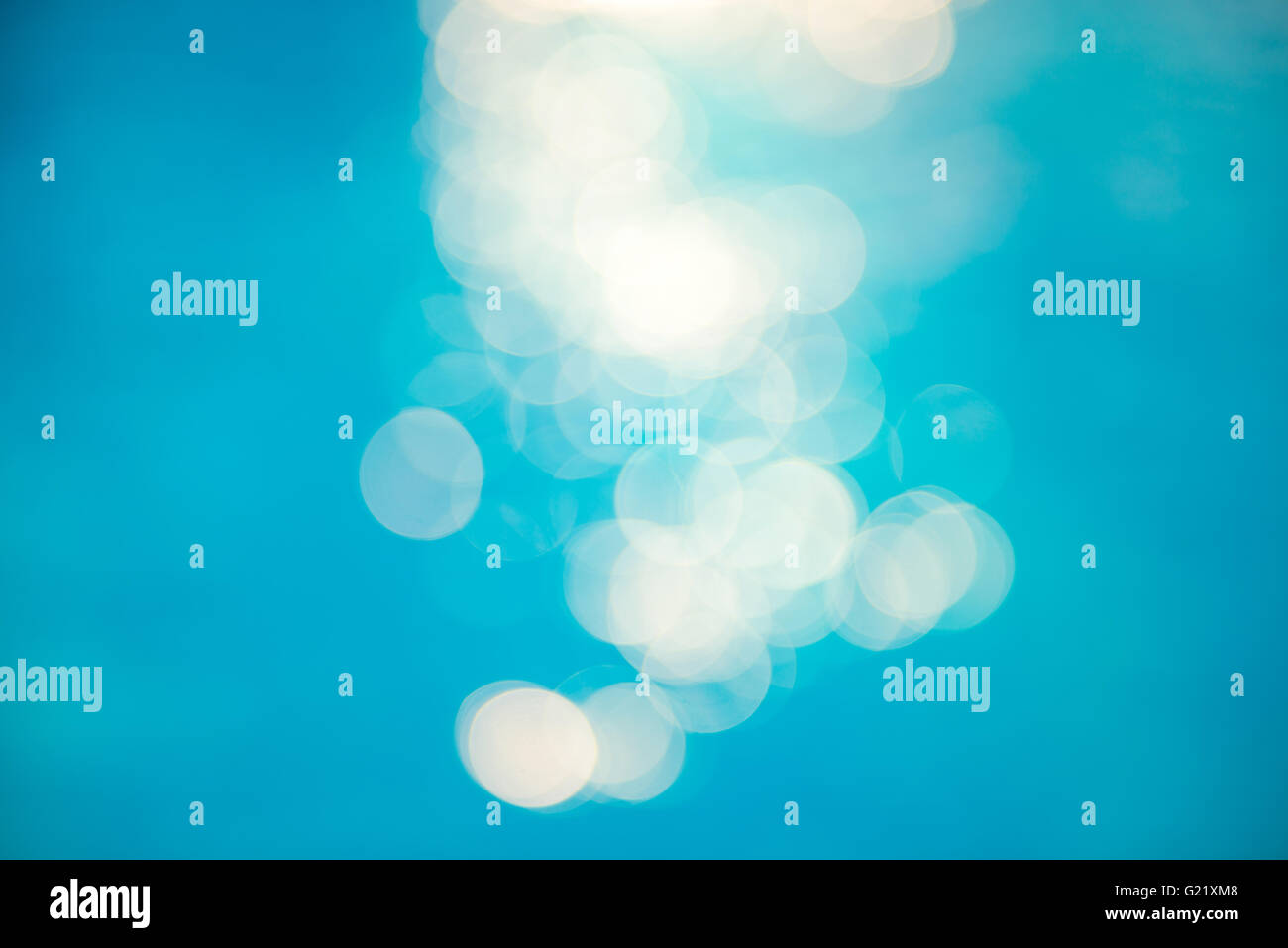 Soft focus bokeh light effects over a rippled, blue water background in ...