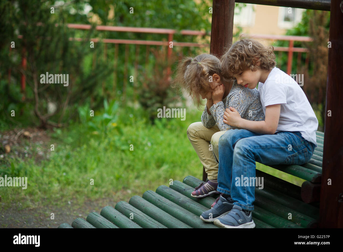 Two sad children sitting on a bench in the yard Stock Photo - Alamy