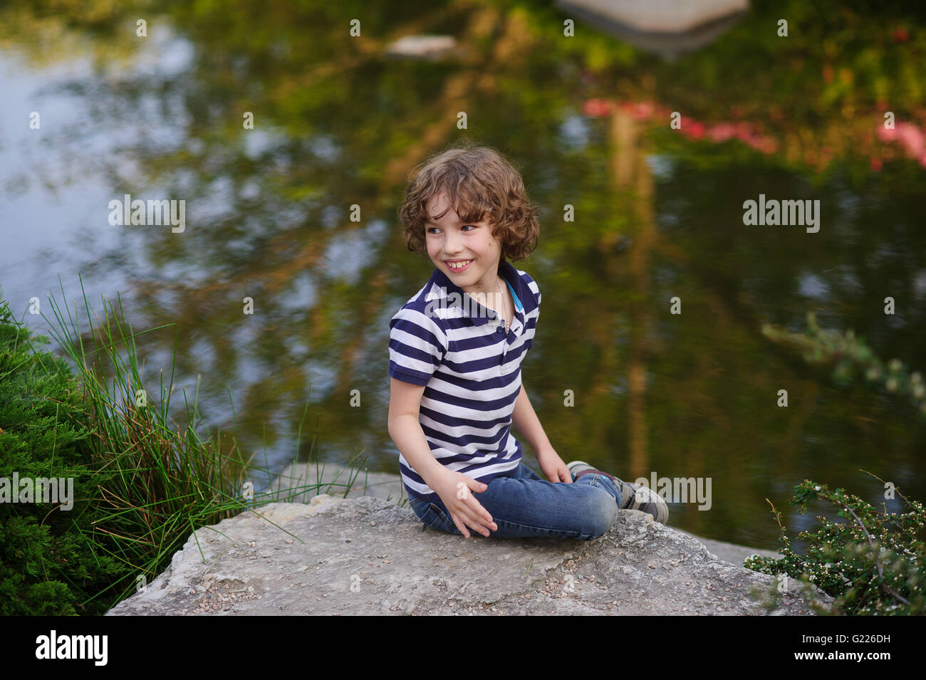Boy sitting on a boulder at the picturesque pond Stock Photo - Alamy