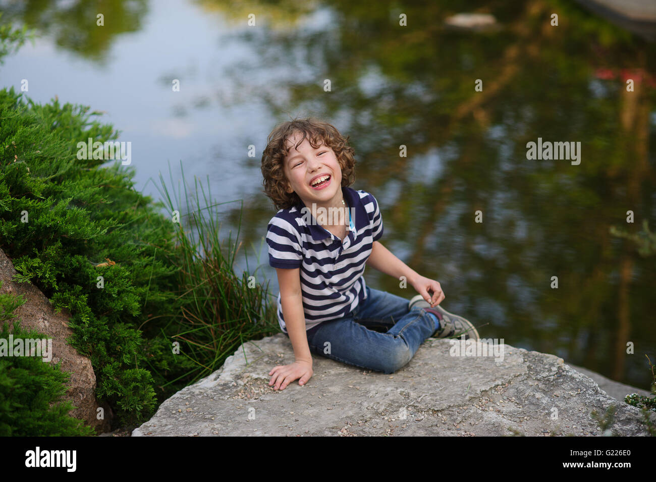 Laughing boy sitting on a boulder near the pond Stock Photo - Alamy