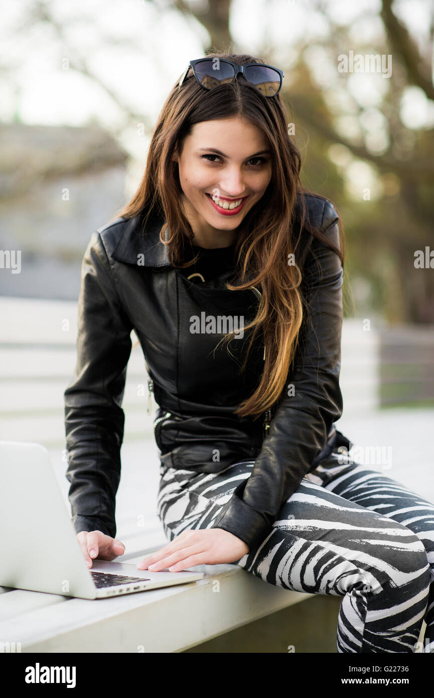 Girl works with laptop computer sitting on a bench in the park looking ...
