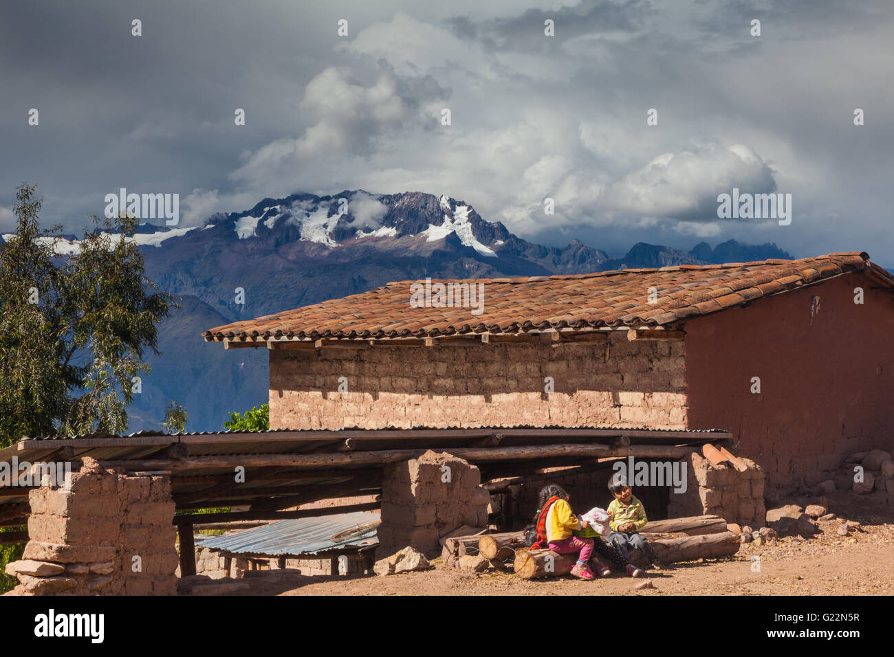 Two children sitting outside an adobe house in the Andean village of ...