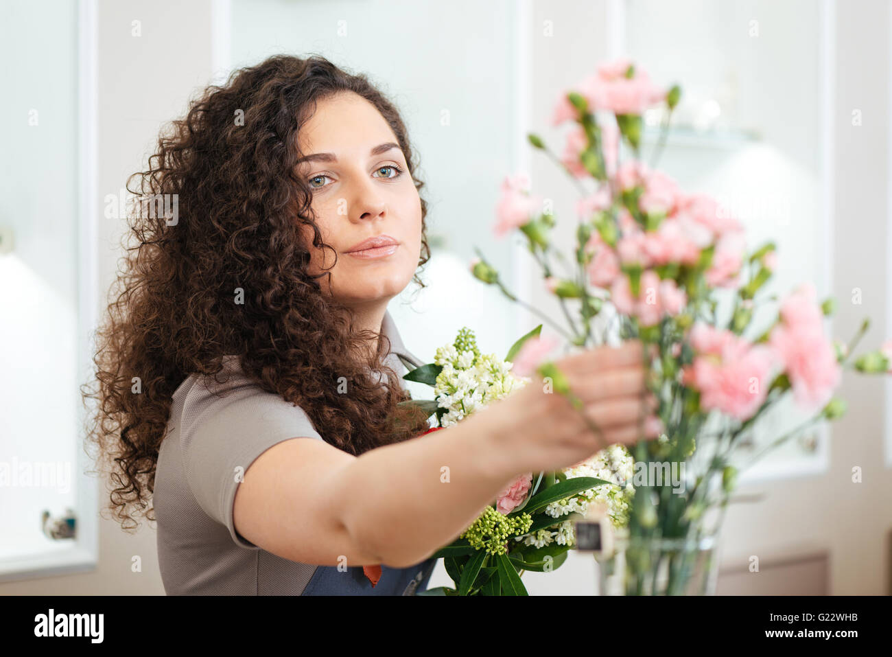 Beautiful concentrated young woman florist taking flowers and making ...