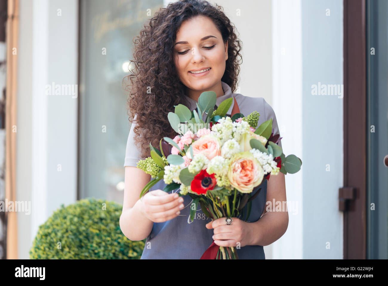 Smiling cute young woman florist with flower bouquet standing in front ...