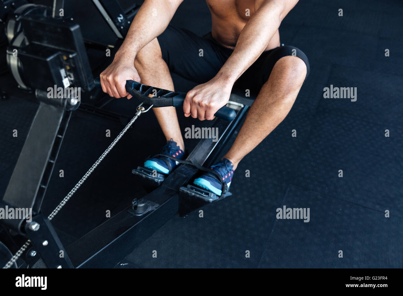 Cropped image of a muscular fitness man using rowing machine in the gym ...