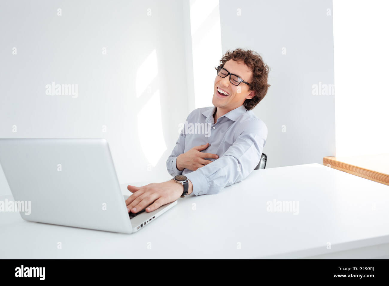Laughing businessman sitting at his workplace in office Stock Photo - Alamy