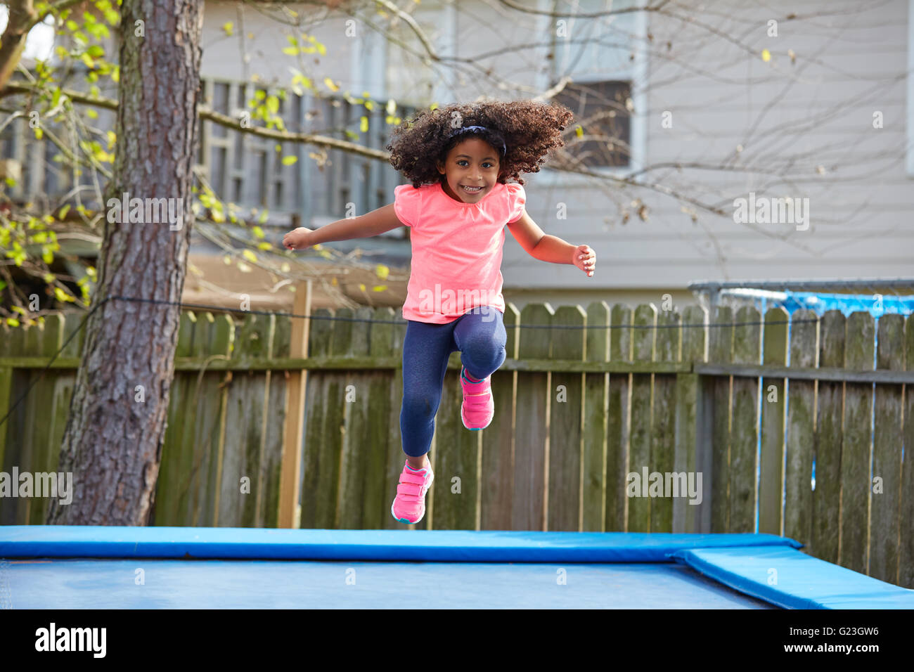 Kid toddler girl jumping on a trampoline playground in the backyard ...