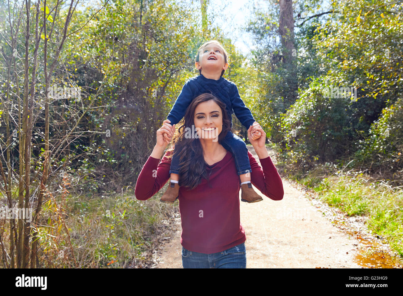 kid boy sitting on mother shoulders walking in the park trail Stock ...