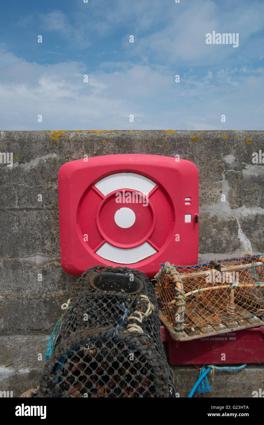 Red and white lifebelt box on the harbour wall with crab and lobster ...
