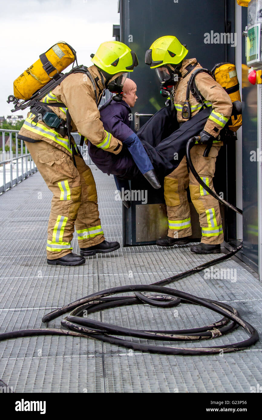 Firefighters wearing breathing apparatus carry a casualty dummy along a ...