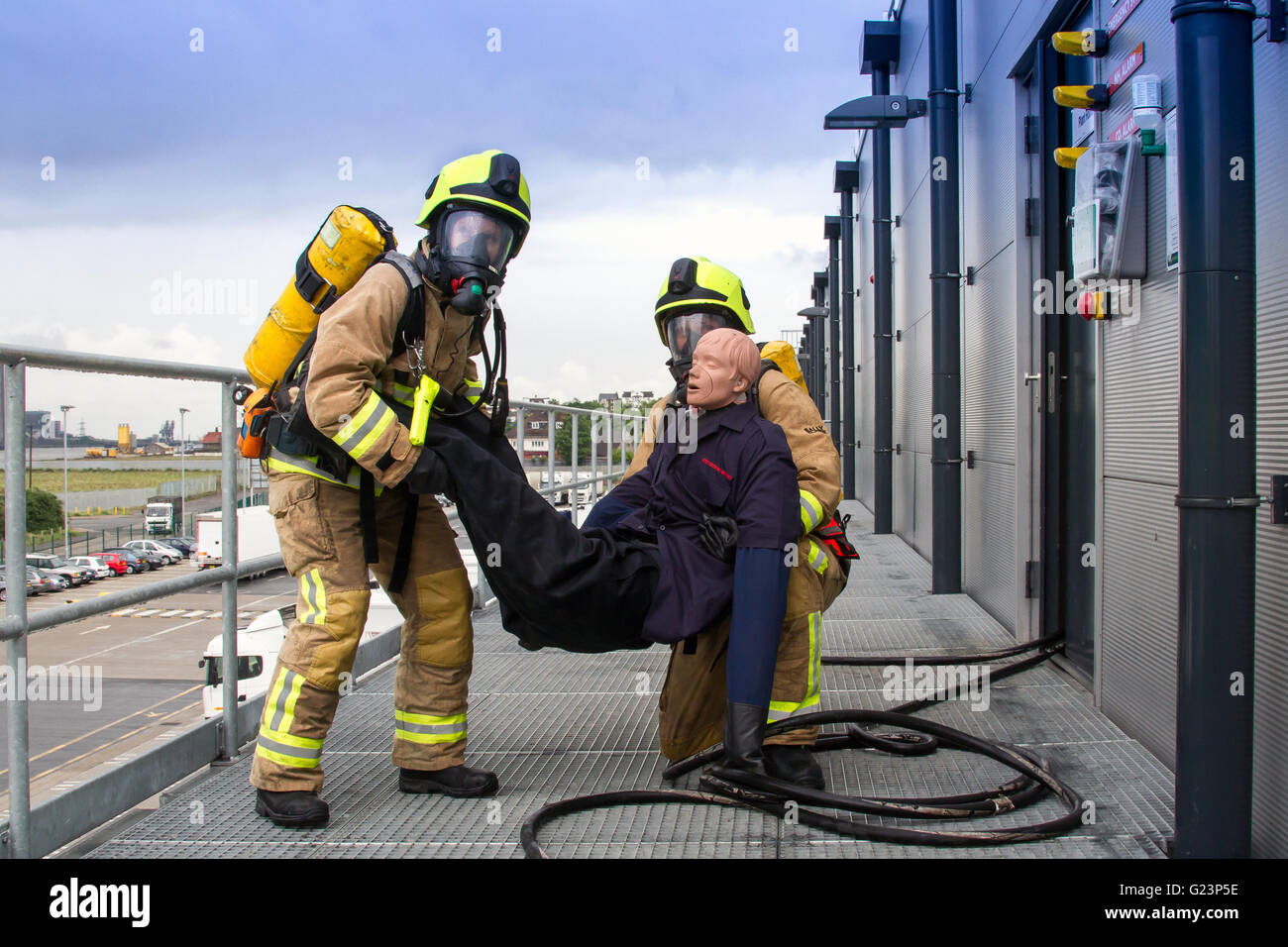 Firefighters wearing breathing apparatus carry a casualty dummy along a ...