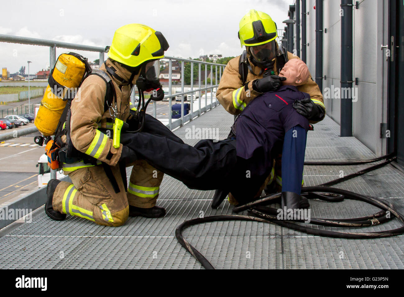 Firefighters wearing breathing apparatus carry a casualty dummy along a ...