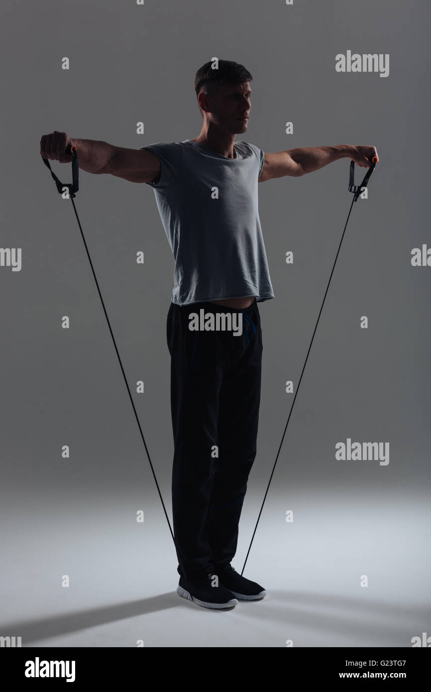 Full length portrait of a sports man workout with expander over gray ...