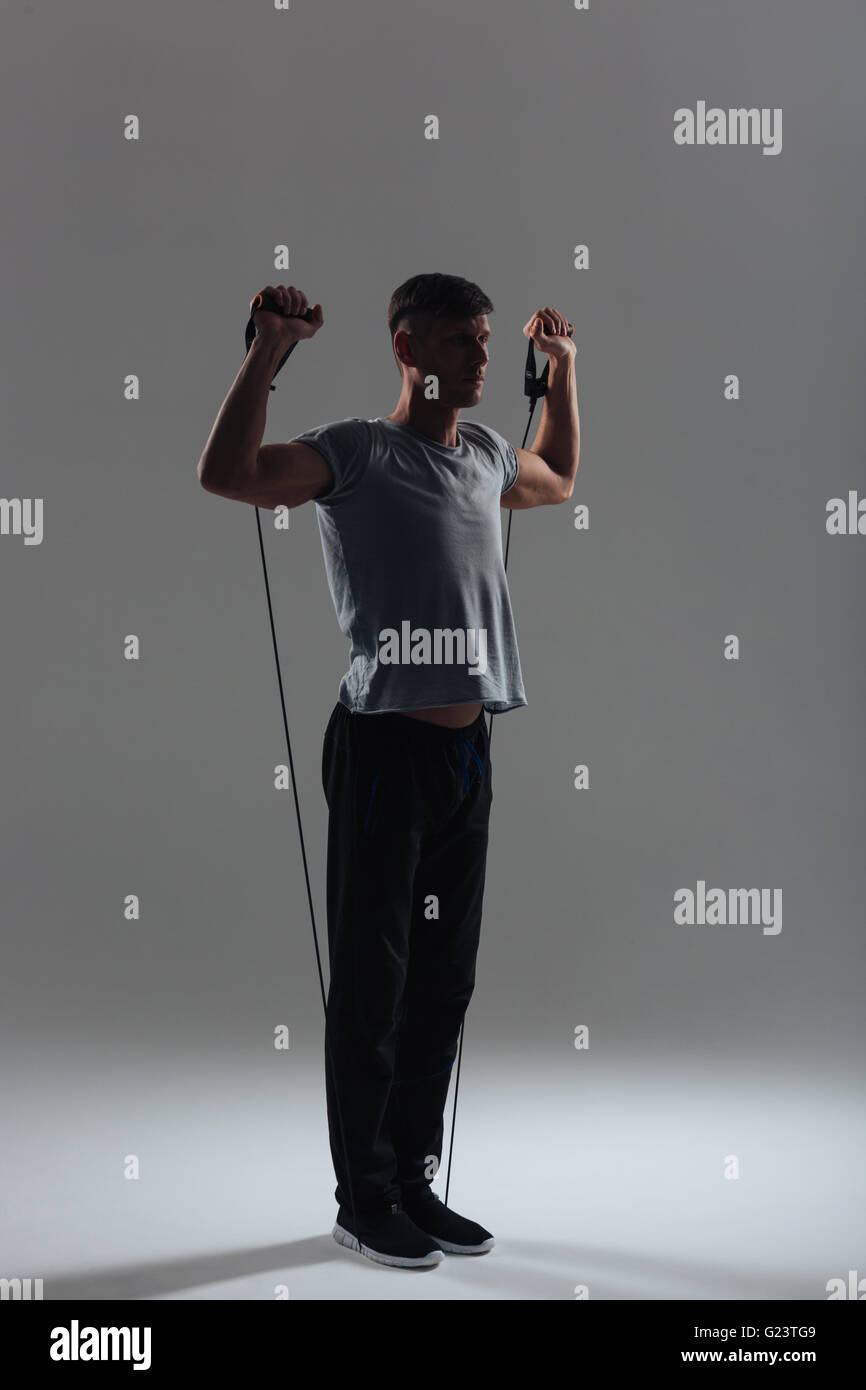 Full length portrait of a fitness man workout with expander over gray ...