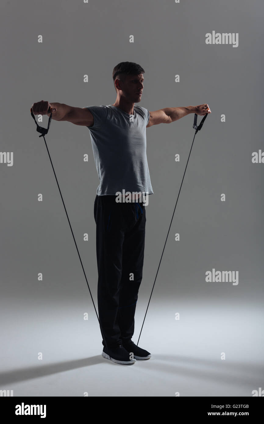 Full length portrait of a fitness man workout with expander over gray ...