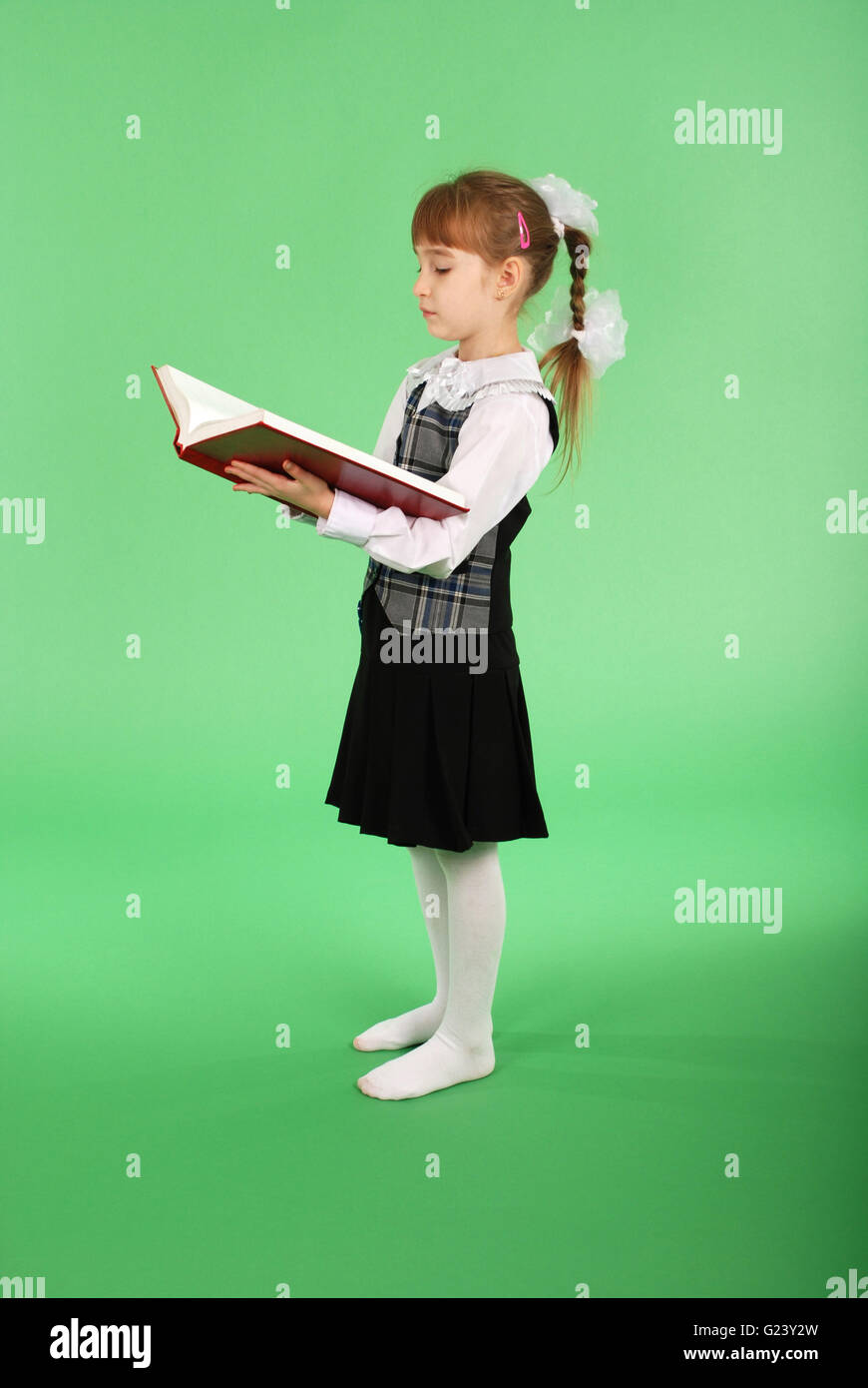 Girl in school uniform reading a book isolated on green Stock Photo - Alamy