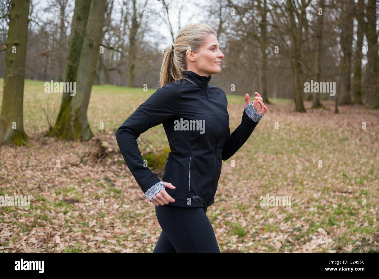 Middle aged woman jogging in an autumnal park, behind a backdrop of ...