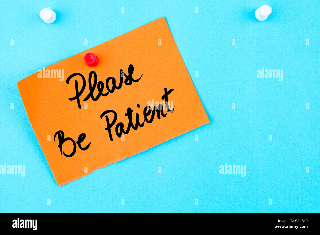 Please Be Patient written on orange paper note pinned on cork board ...