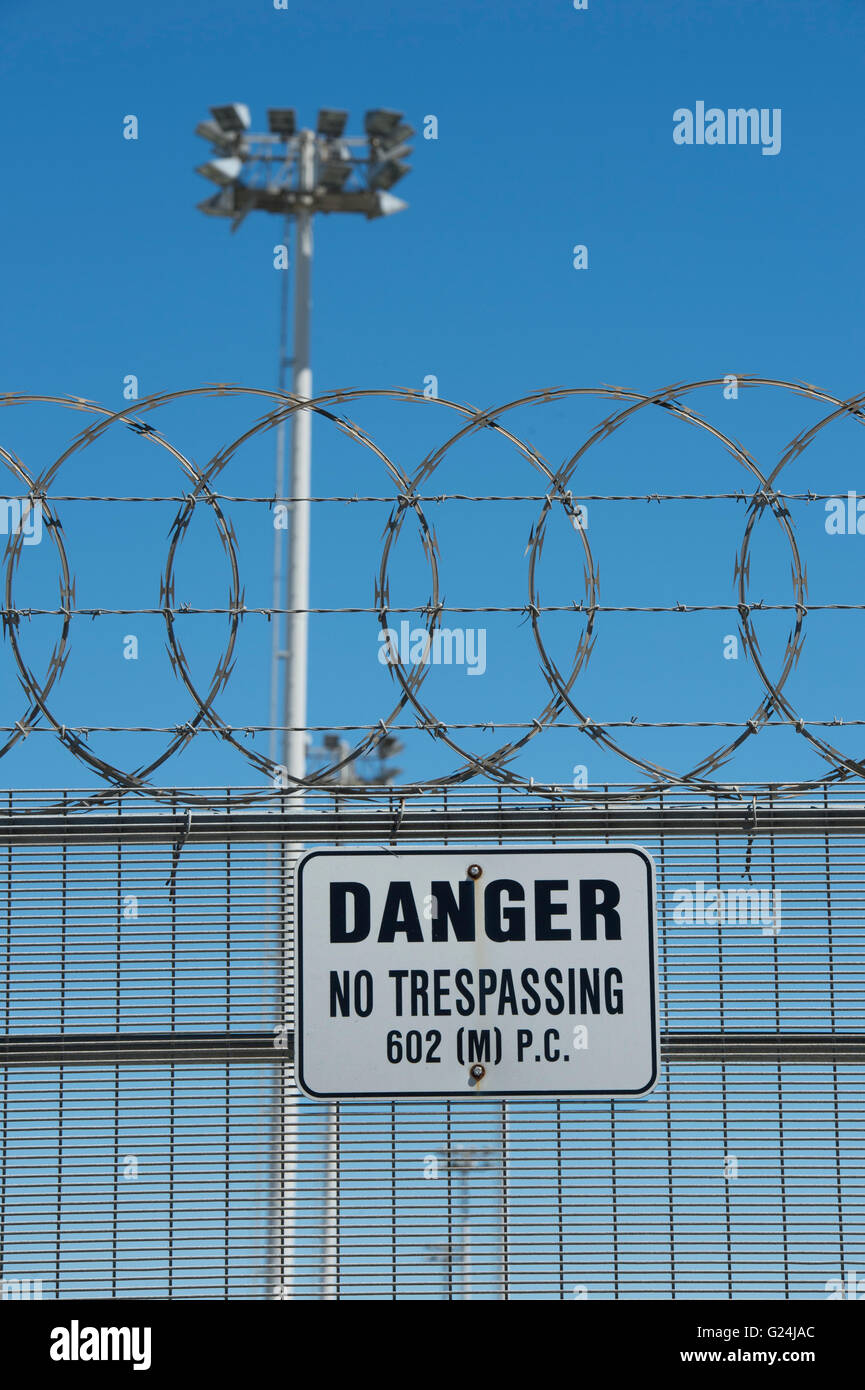Security fence topped with Razor wire loops. Sign saying DANGER NO ...