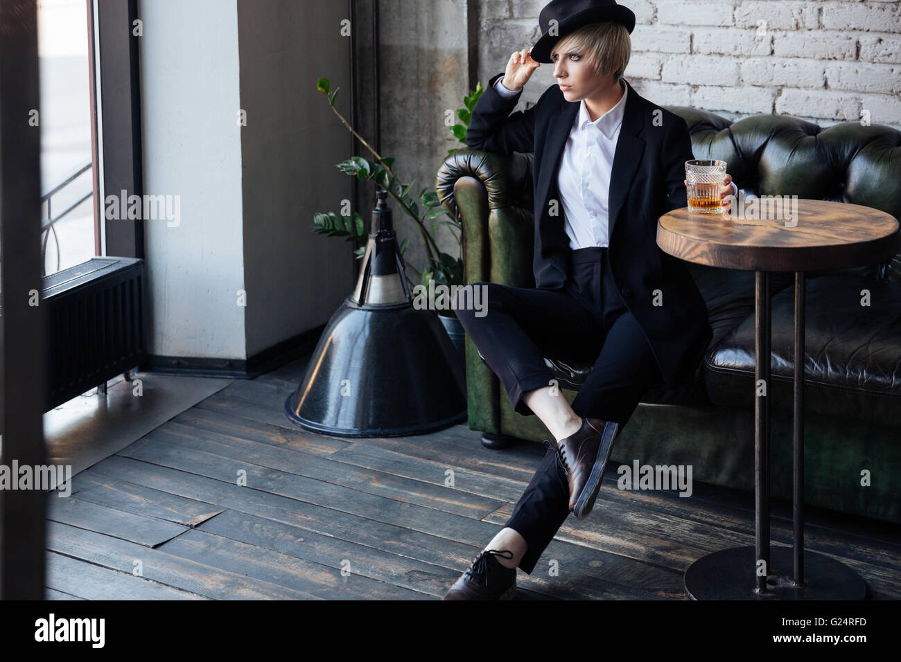 Blonde hipster girl sitting on a couch with her legs crossed in a cafe ...