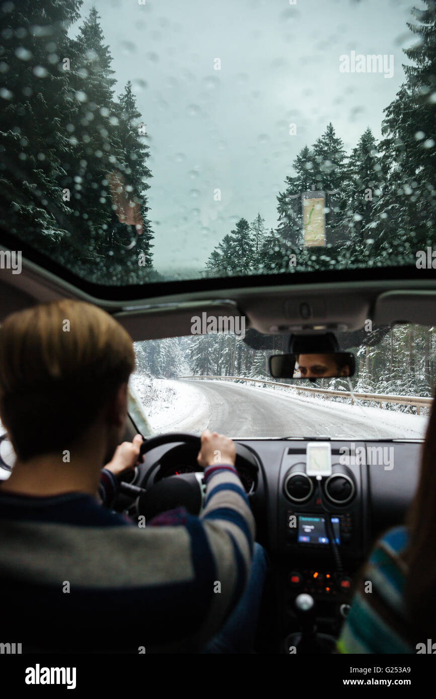 Back view of handsome man driving in car through the winter forest ...