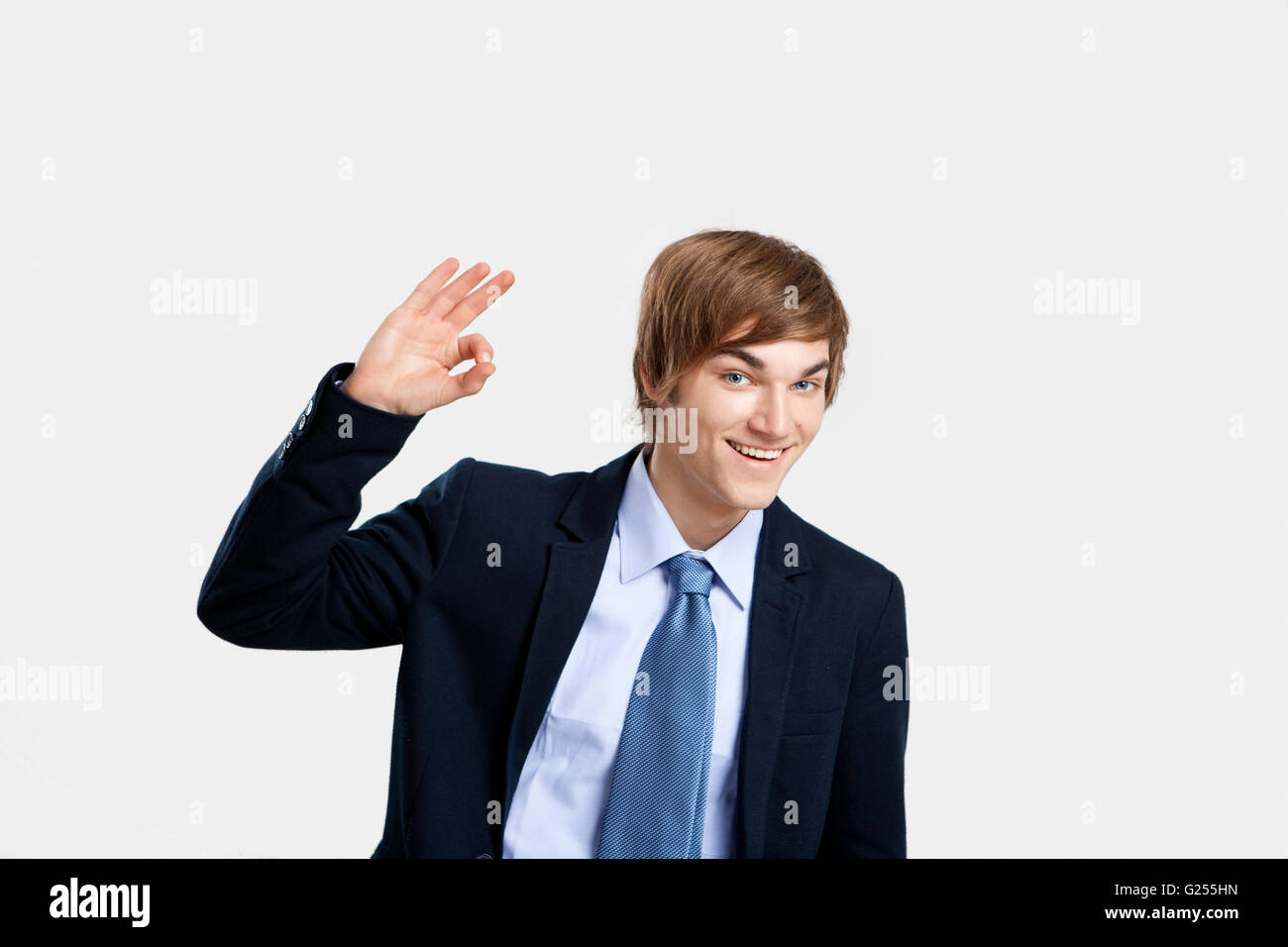 Young businessman doing a Okay signal to the camera, over a gray ...