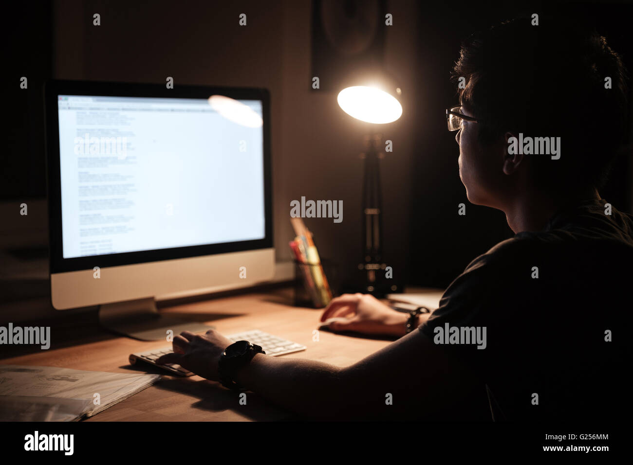 Concentrated young asian man using computer sitting in dark room at ...