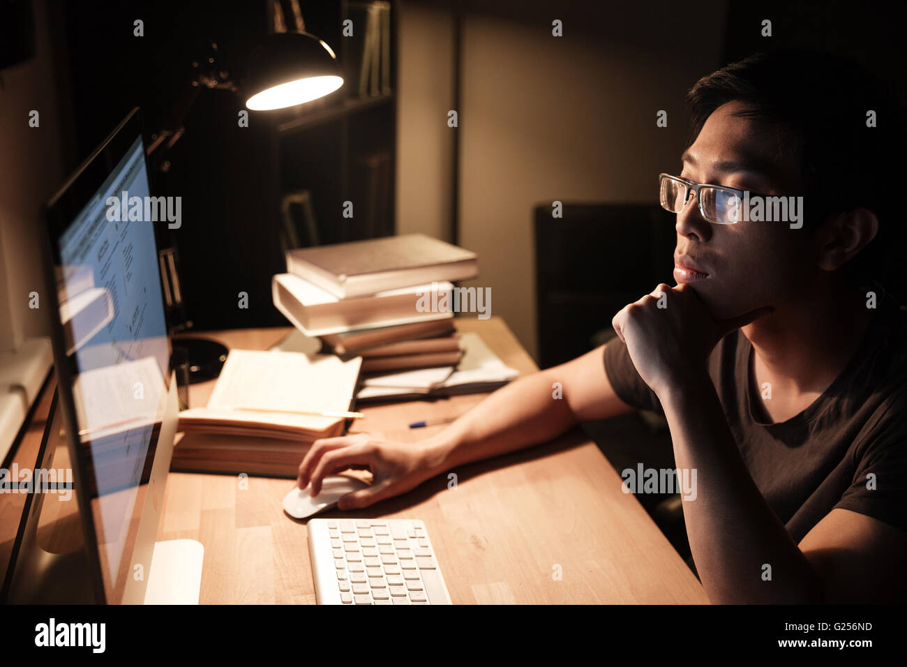 Pensive asian young man in glasses working with computer and thinking ...