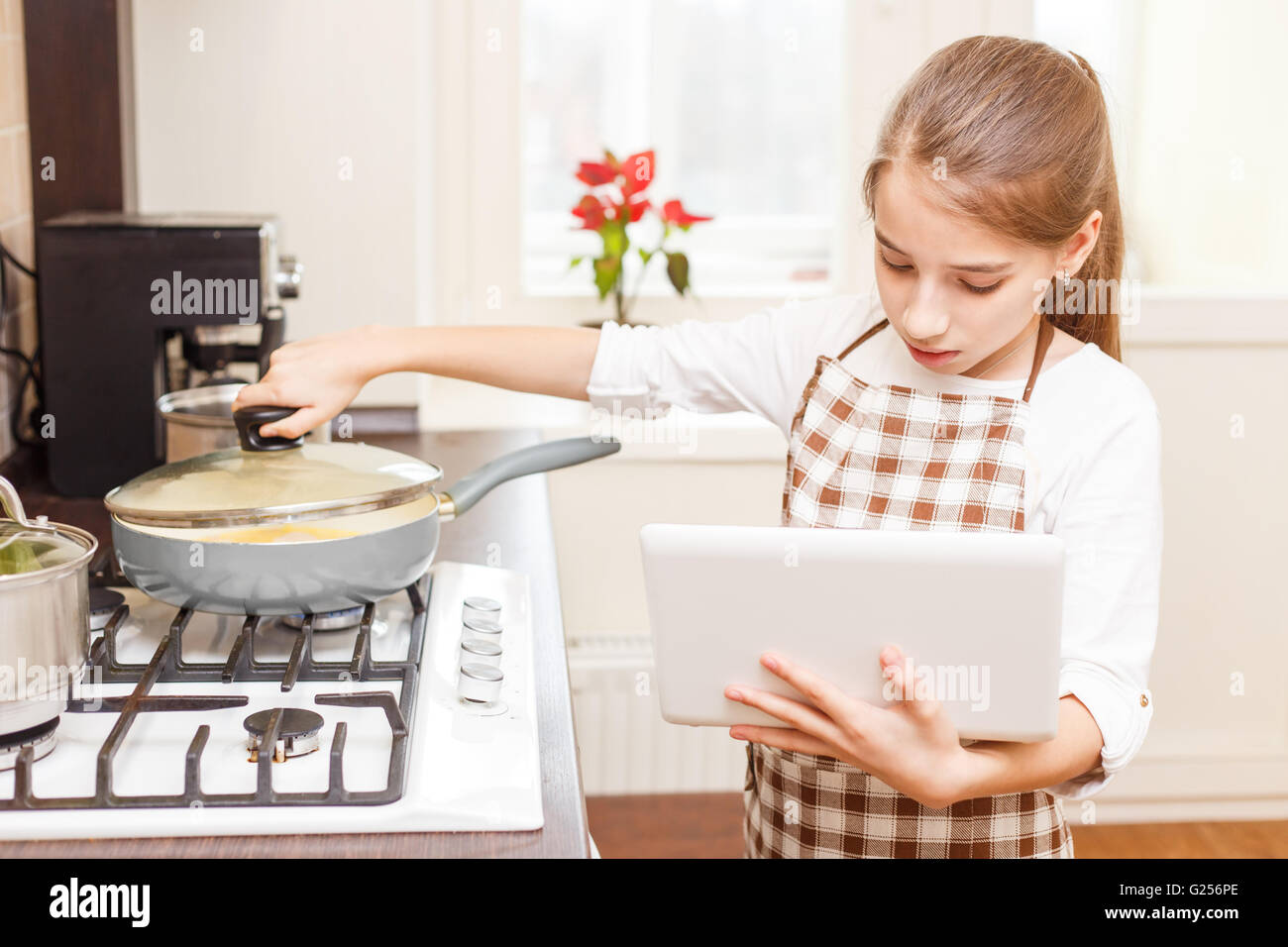 Small teenage girl cooking on cooker with laptop. Teenager girl ...