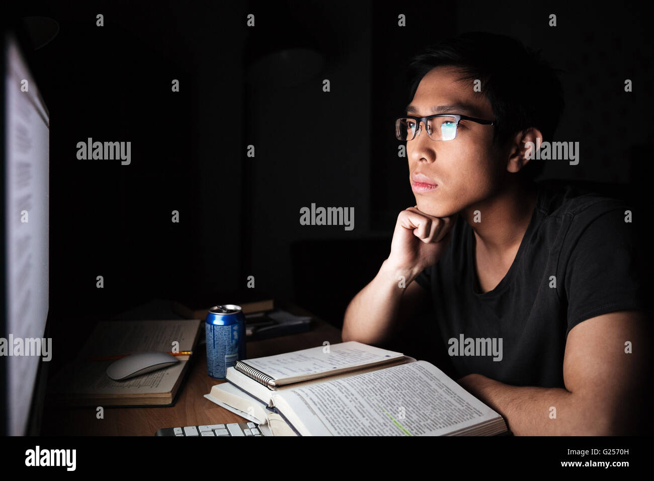 Serious asian young man sitting and studying with books and computer in ...