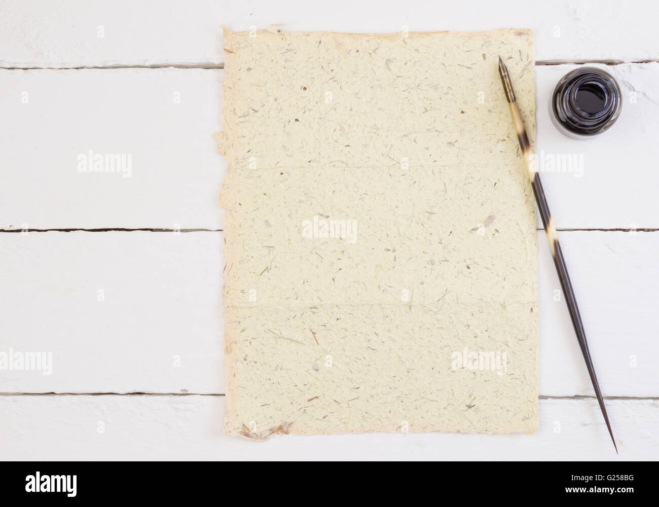 Yellow hand made blank paper, quill pen and ink on rustic white wood ...