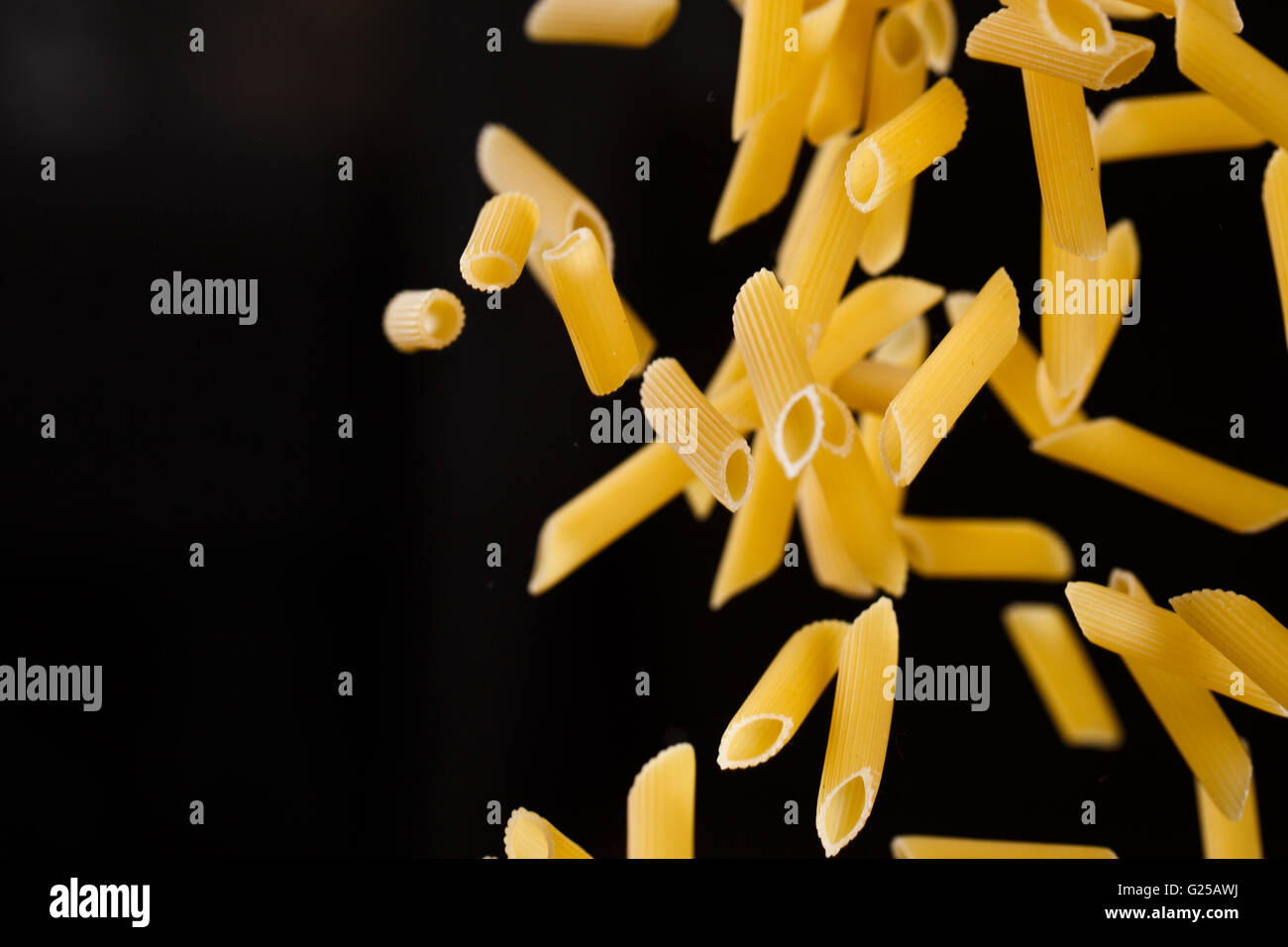 Falling penne pasta. Flying yellow raw macaroni over black background ...